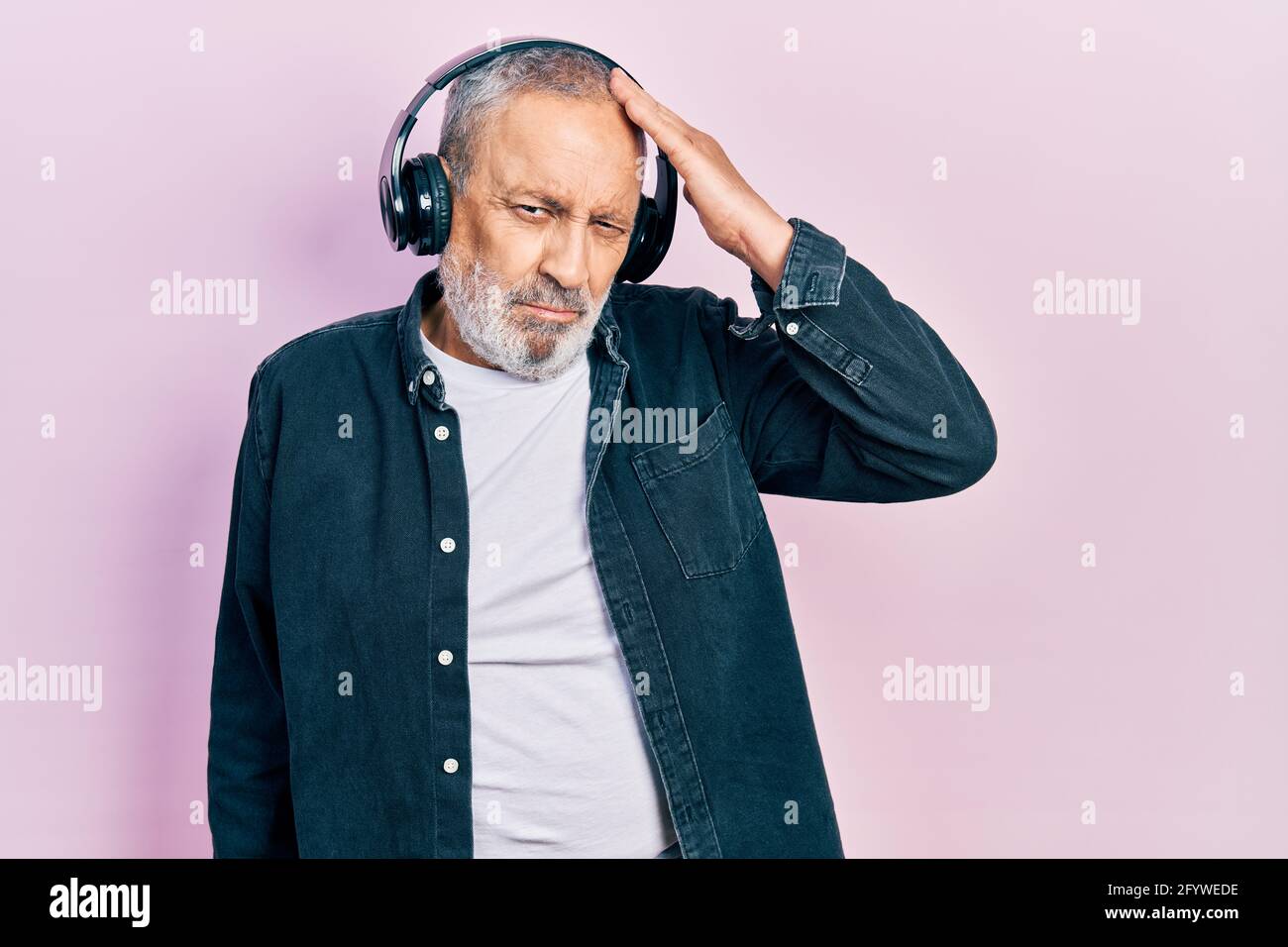 Handsome senior man with beard listening to music using headphones ...