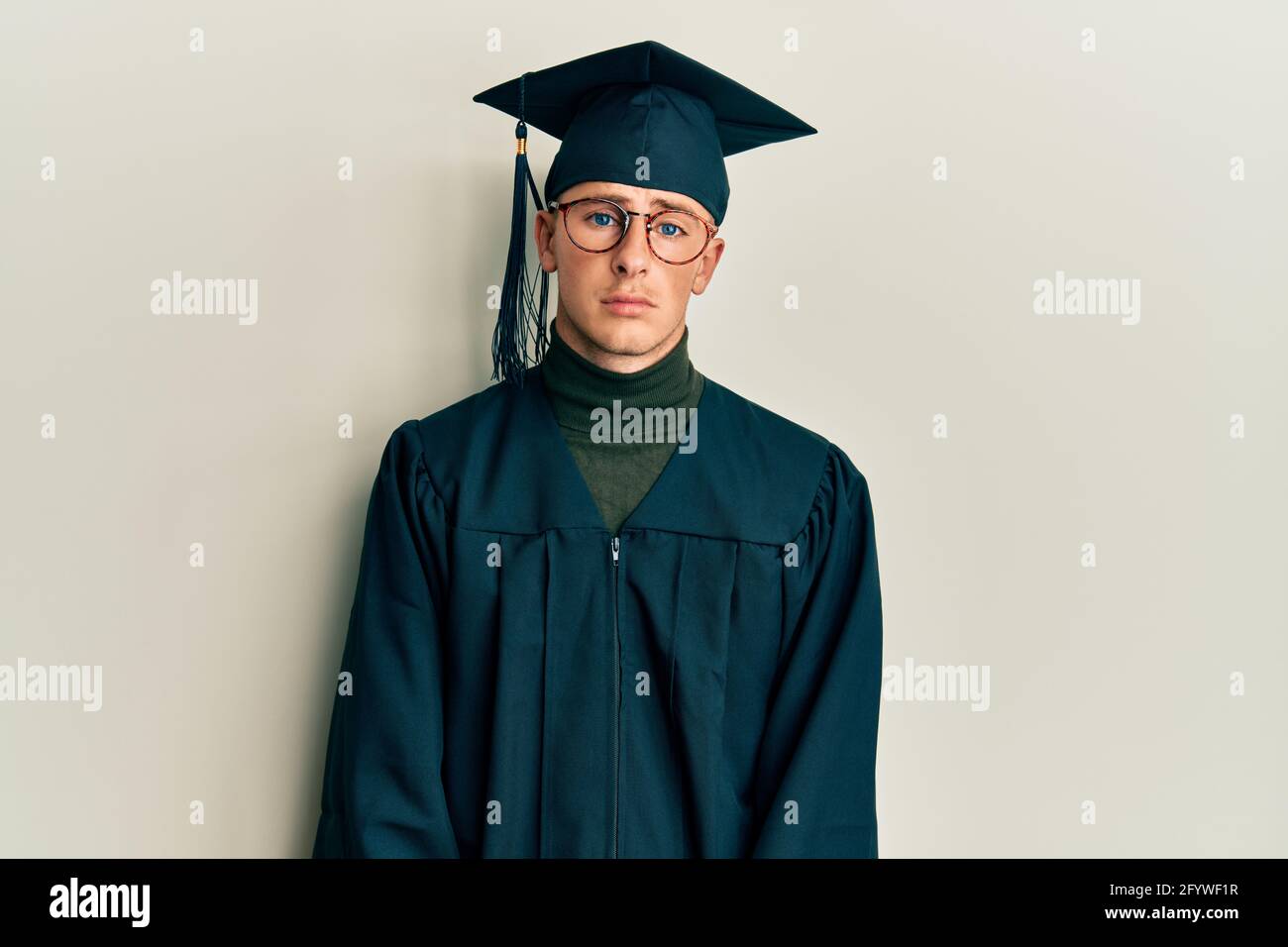 Young caucasian man wearing graduation cap and ceremony robe depressed ...