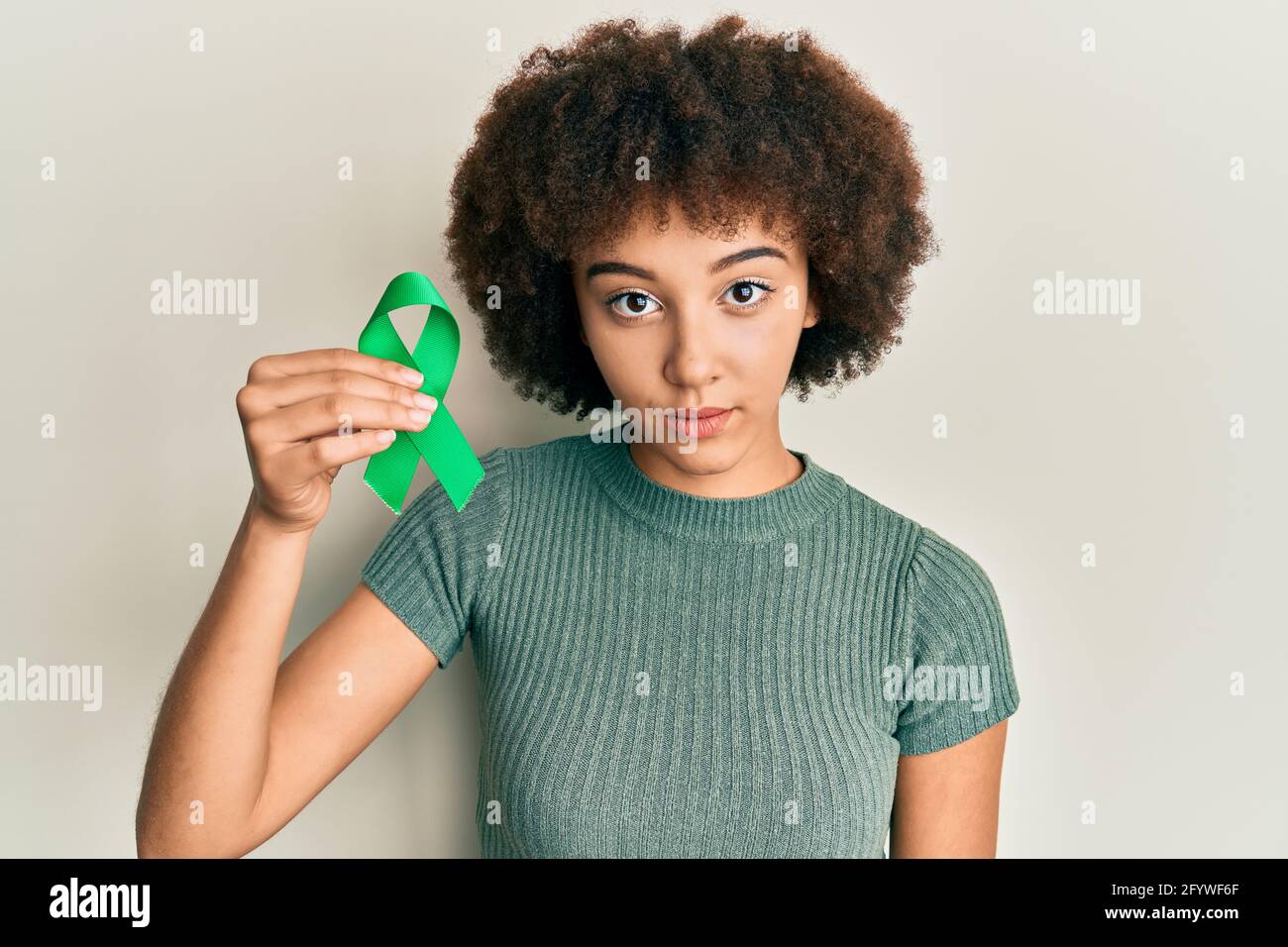Young hispanic girl holding support green ribbon thinking attitude and ...