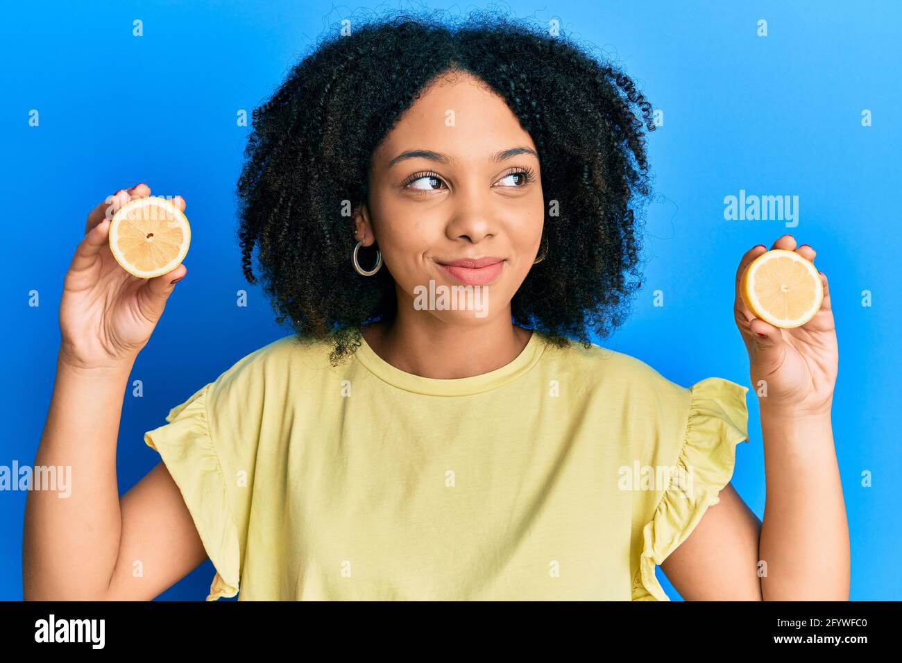 Young african american girl holding lemon smiling looking to the side ...
