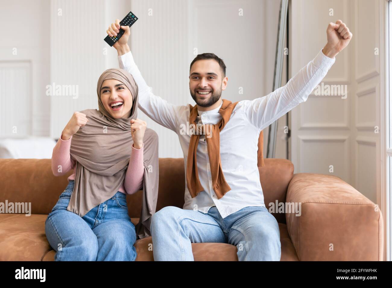 Emotional Muslim Couple Shaking Fists Watching TV At Home Stock Photo ...