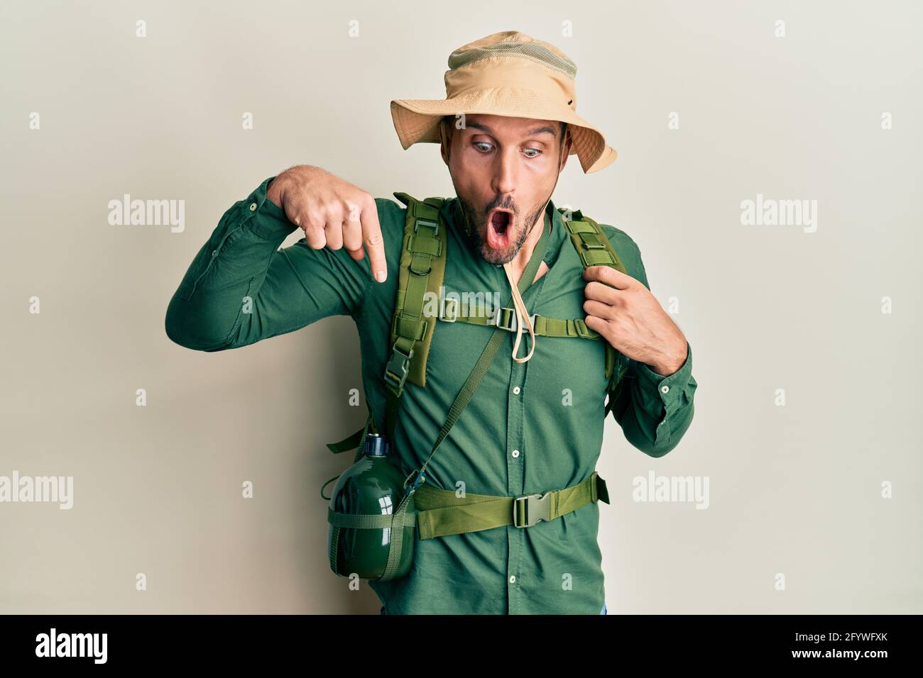 Handsome man with beard wearing explorer hat and backpack pointing down ...
