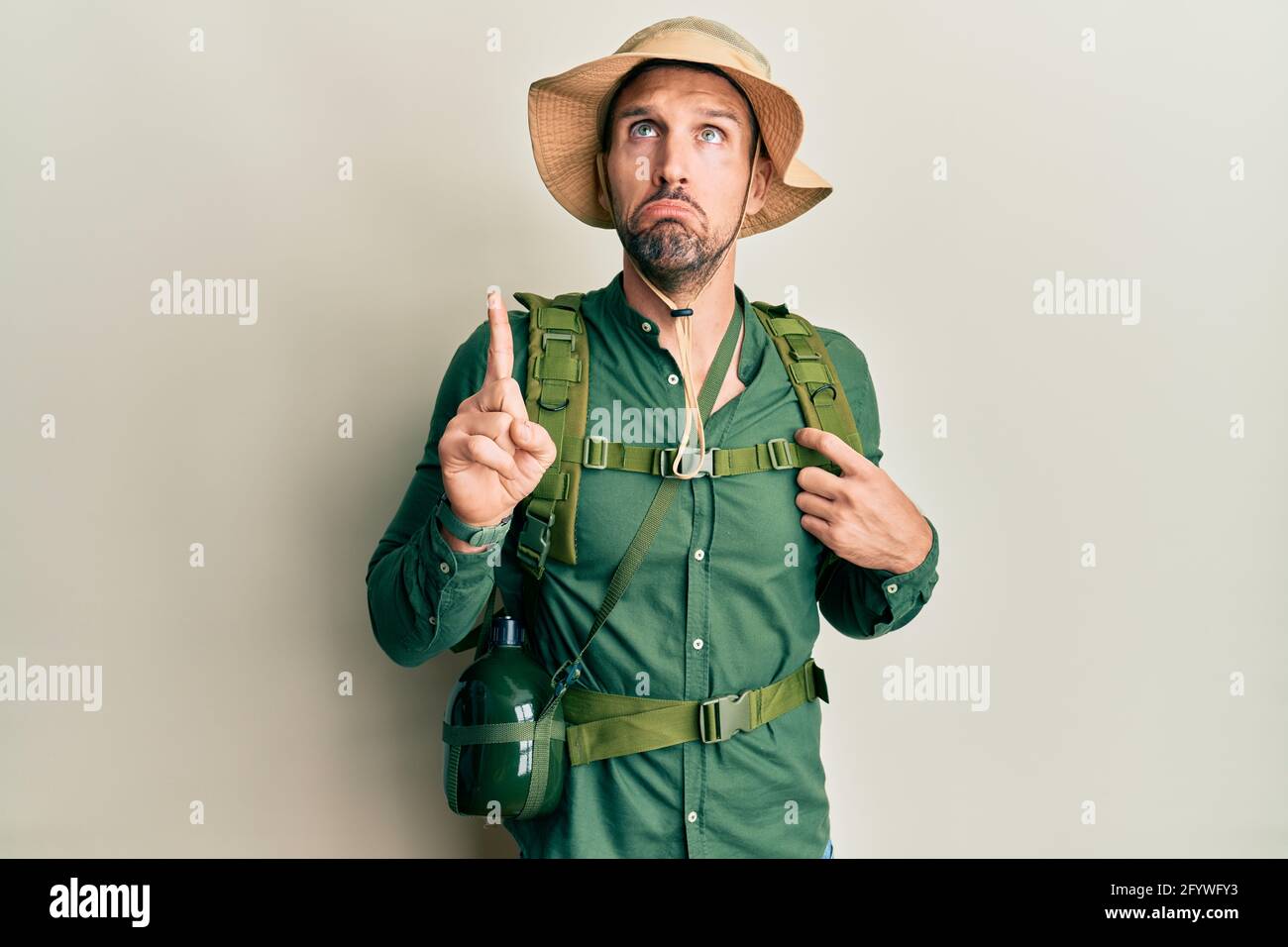 Handsome man with beard wearing explorer hat and backpack pointing up ...