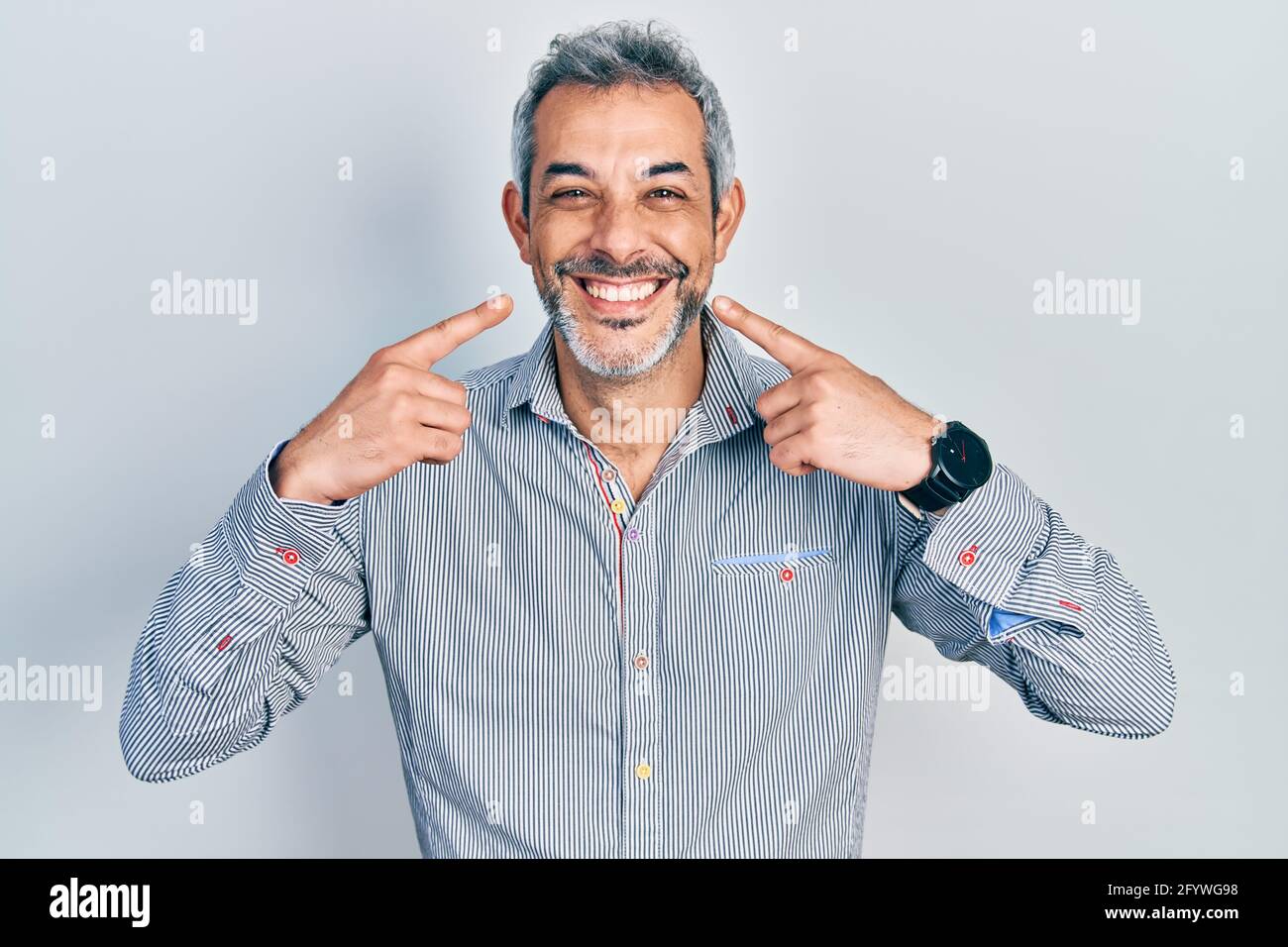 Handsome middle age man with grey hair pointing mouth with fingers ...