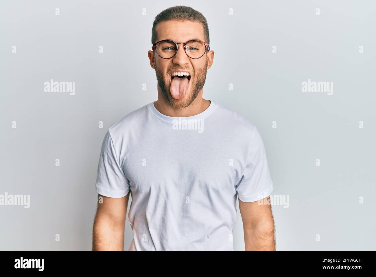 Young caucasian man wearing casual clothes and glasses sticking tongue ...