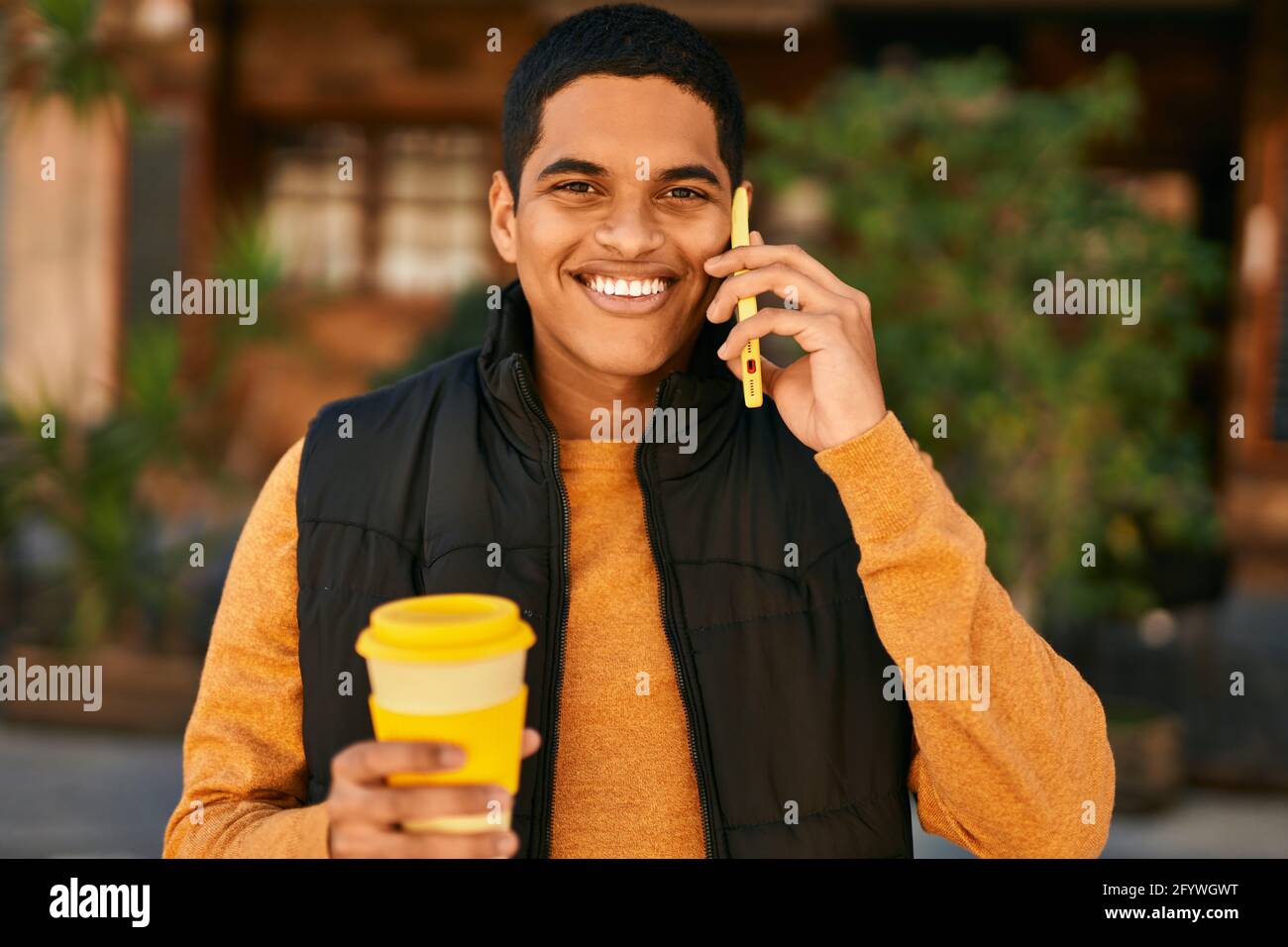 Young latin man talking on the smartphone and drinking coffee at the ...