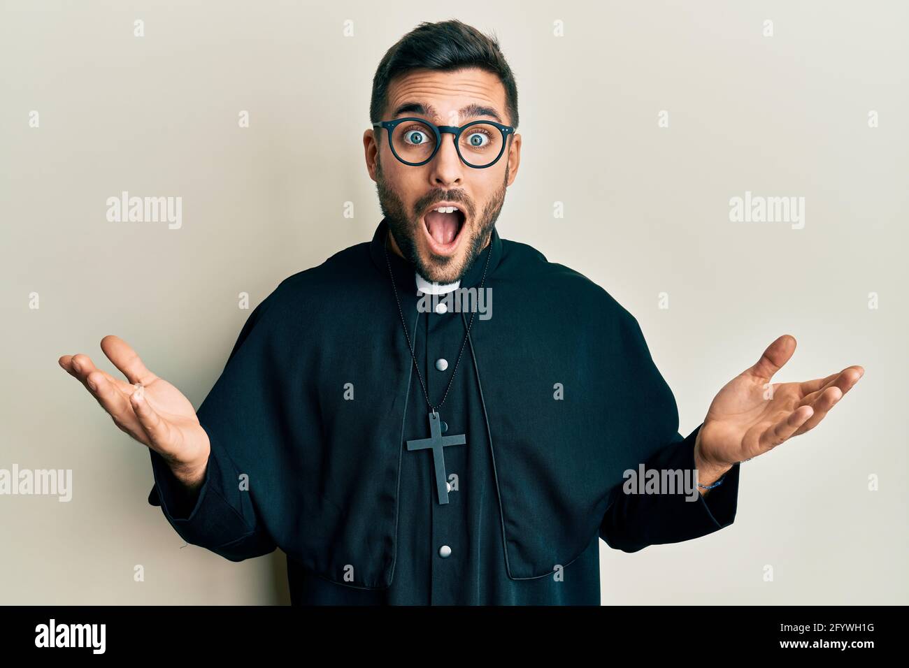 Young hispanic priest man standing over white background celebrating ...