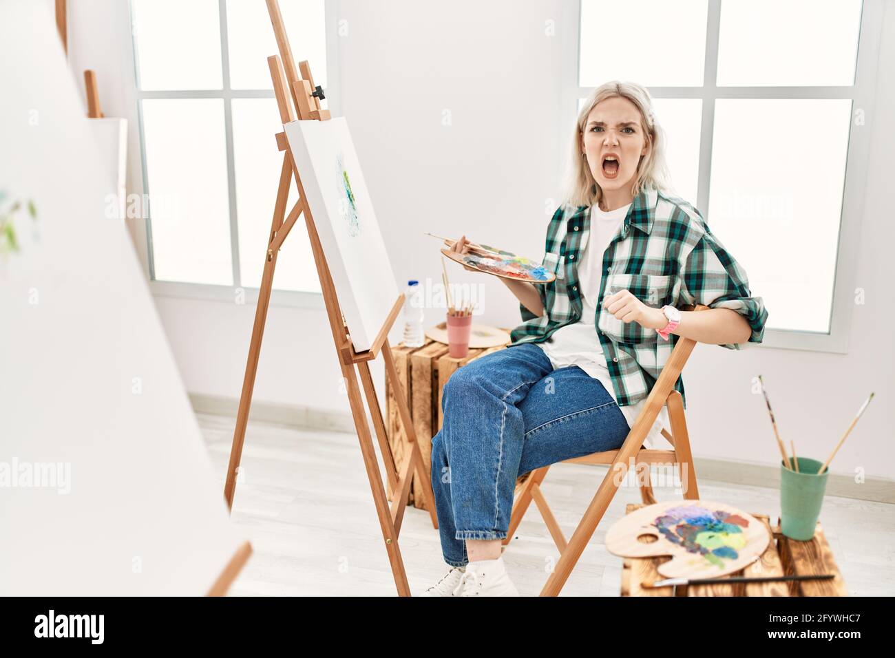 Young artist woman painting on canvas at art studio angry and mad ...
