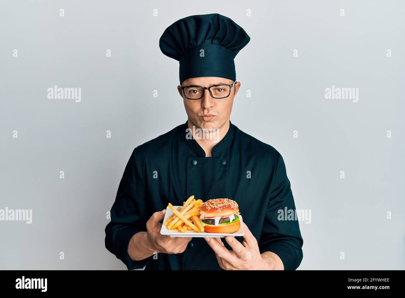 Handsome young man chef holding burger with fries depressed and worry ...