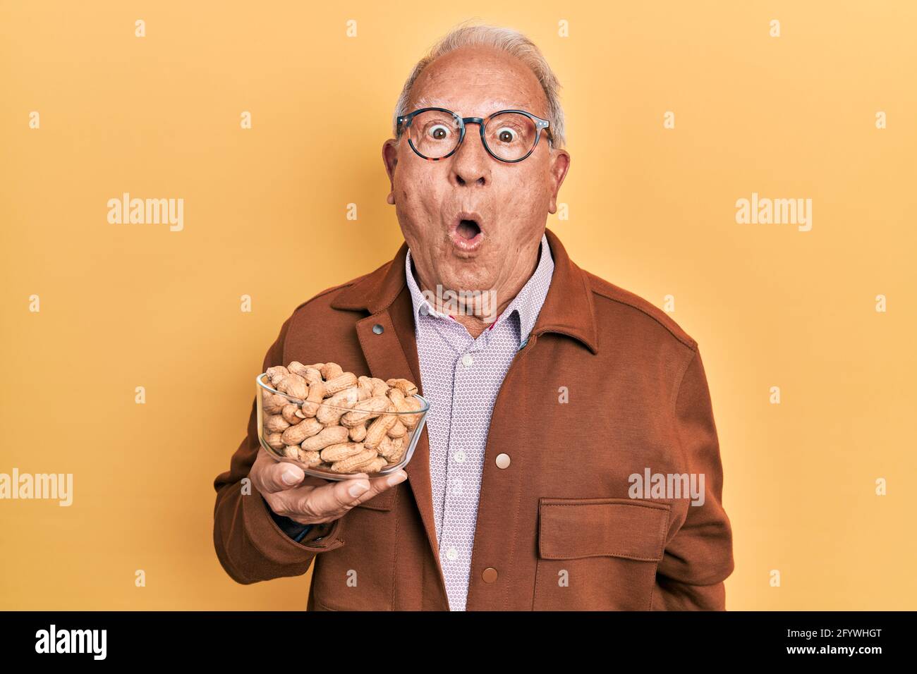 Senior man with grey hair holding peanuts scared and amazed with open ...