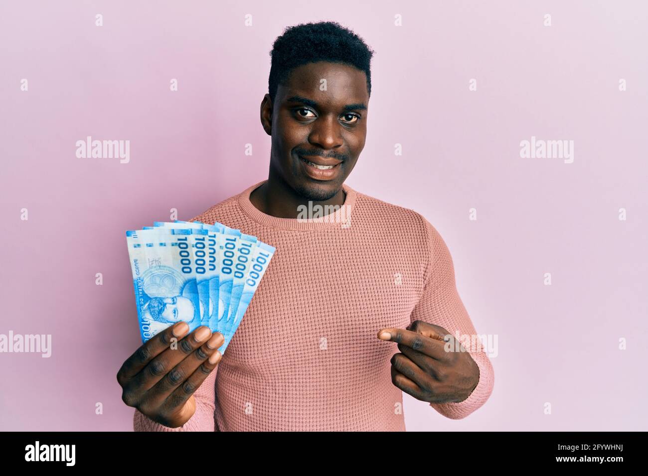 Handsome black man holding 10000 chilean pesos smiling happy pointing ...