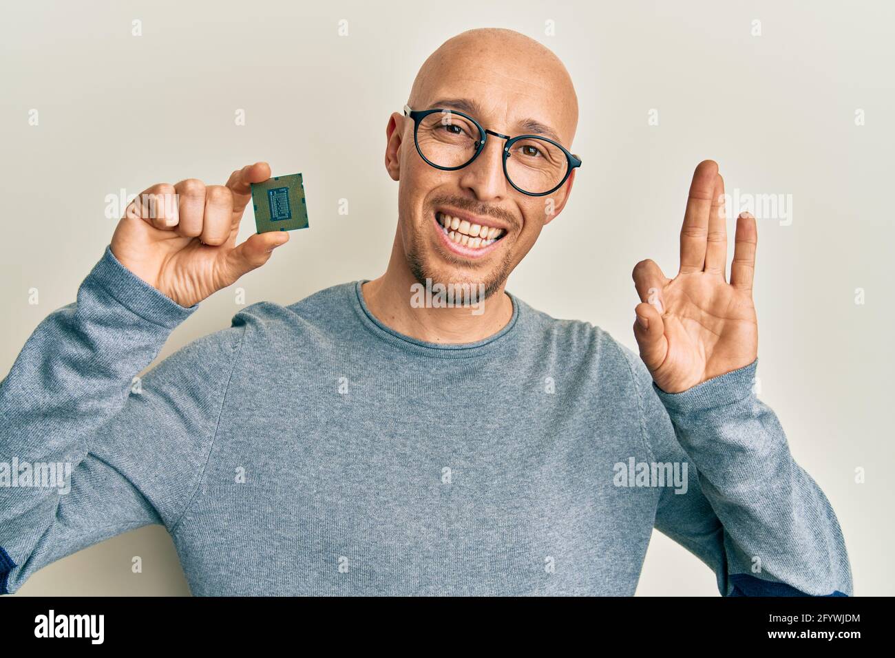 Bald man with beard holding cpu computer processor doing ok sign with ...