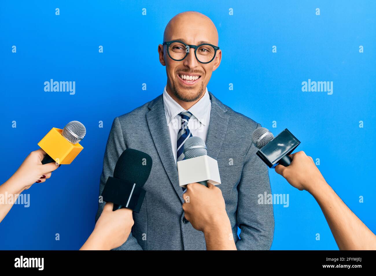 Bald man with beard being interviewed by reporters holding microphones ...
