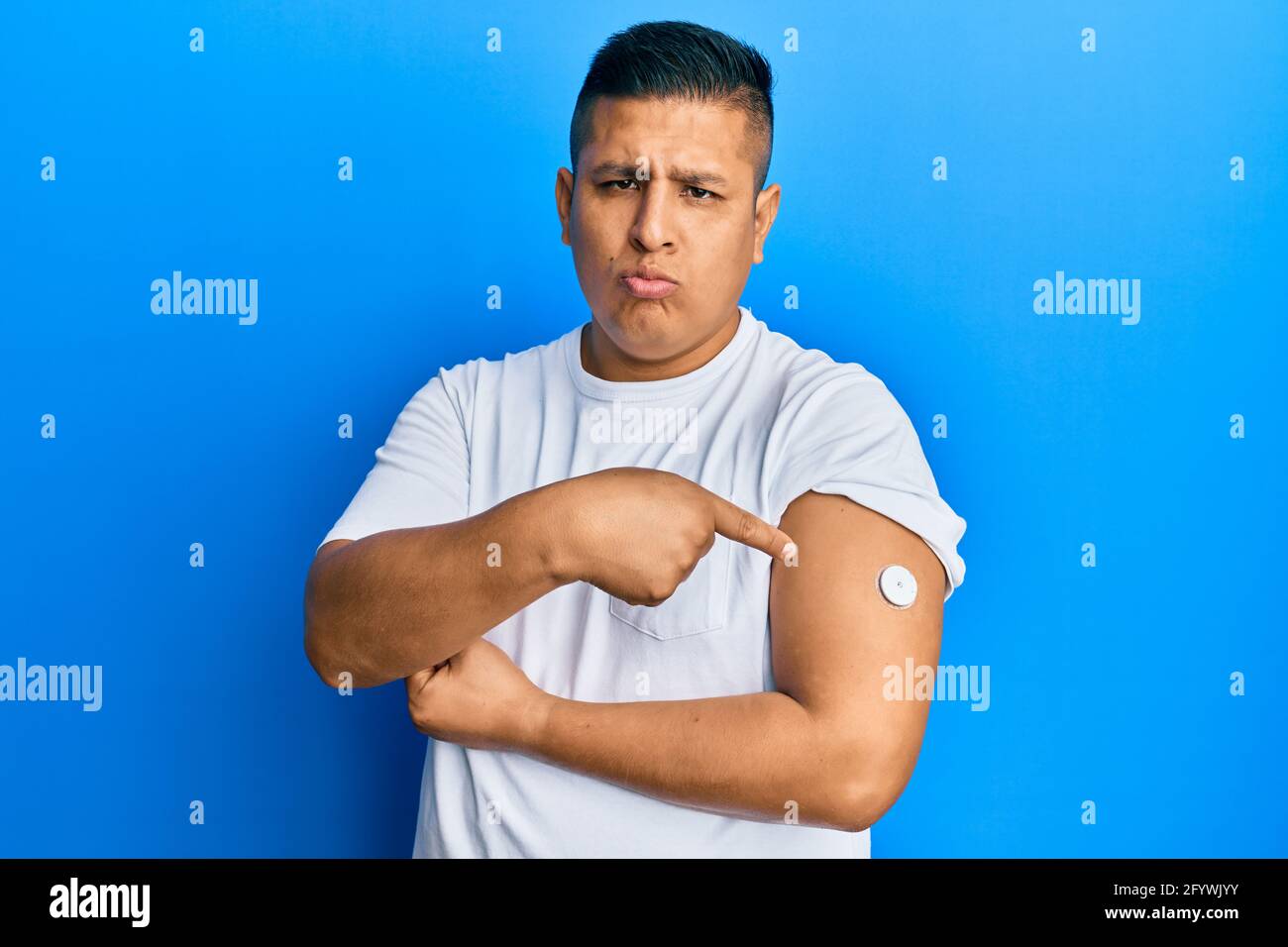 Young latin man using glucose meter button on arm depressed and worry ...