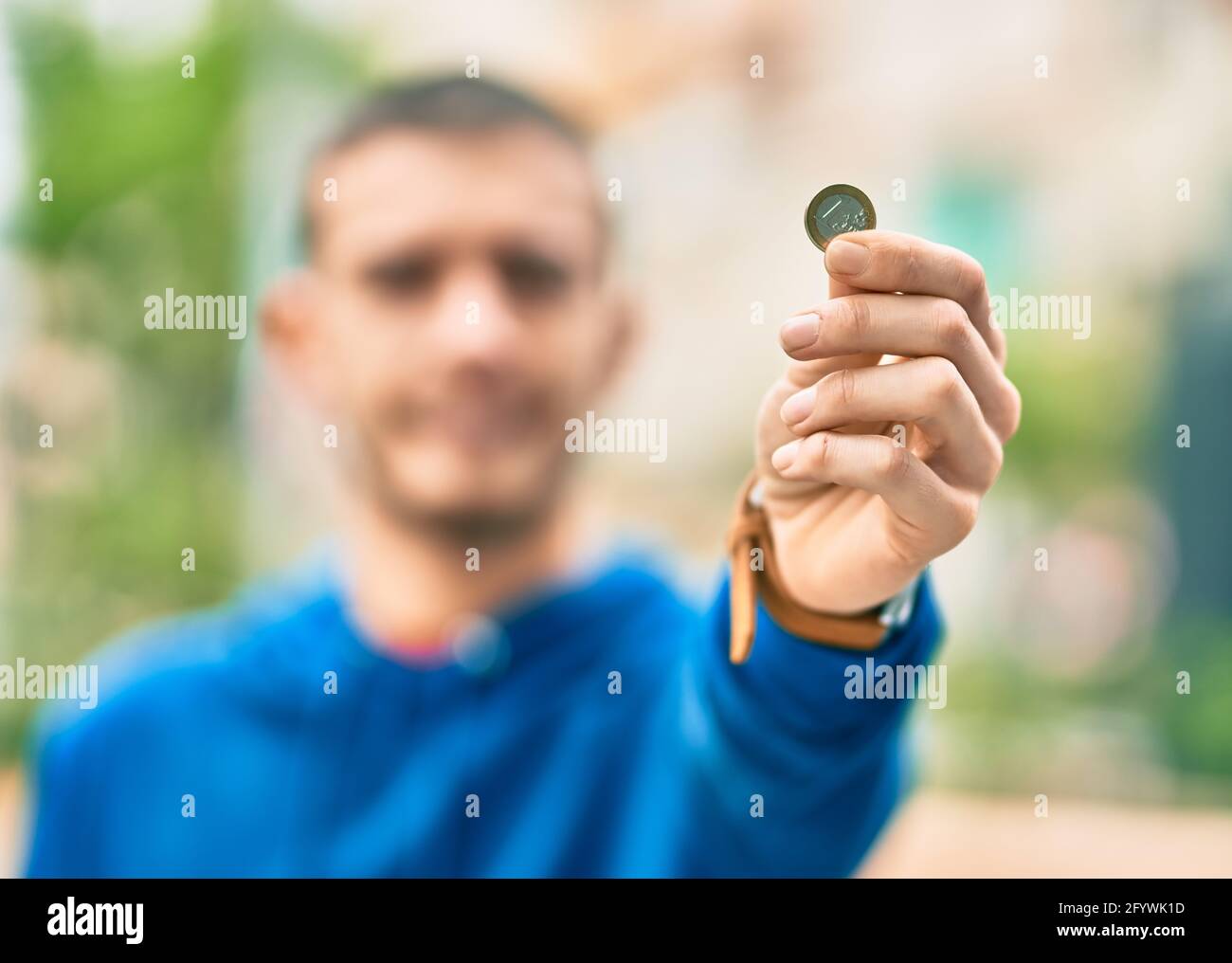 Young hispanic man smiling happy holding 1 euro coin at the city Stock ...