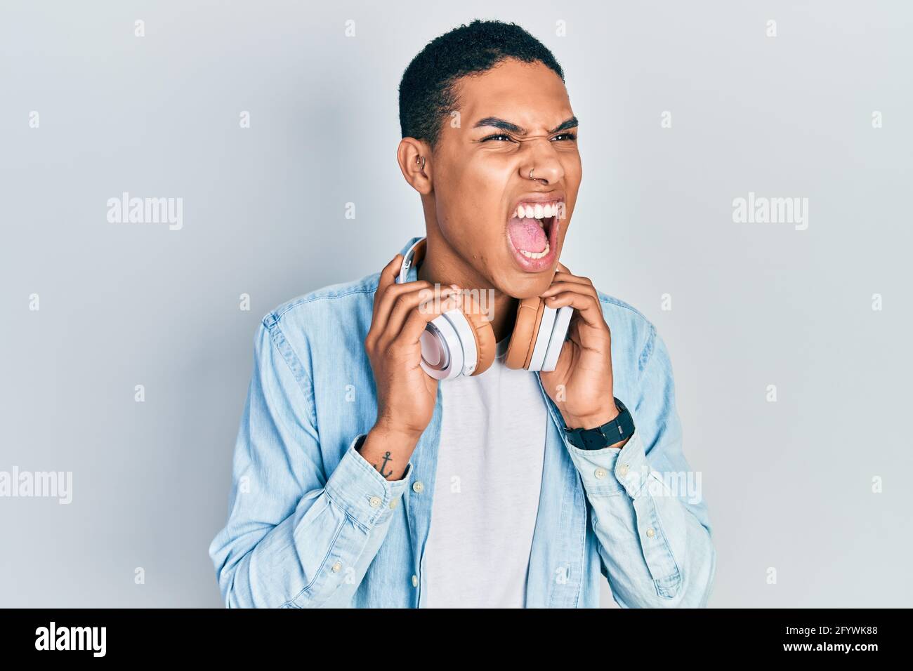 Young african american guy listening to music using headphones angry ...