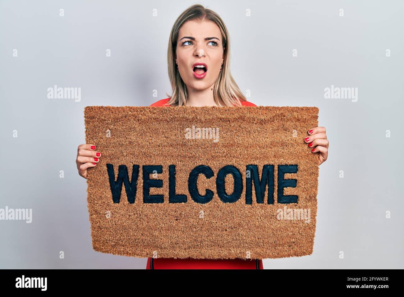 Beautiful caucasian woman holding welcome doormat angry and mad ...
