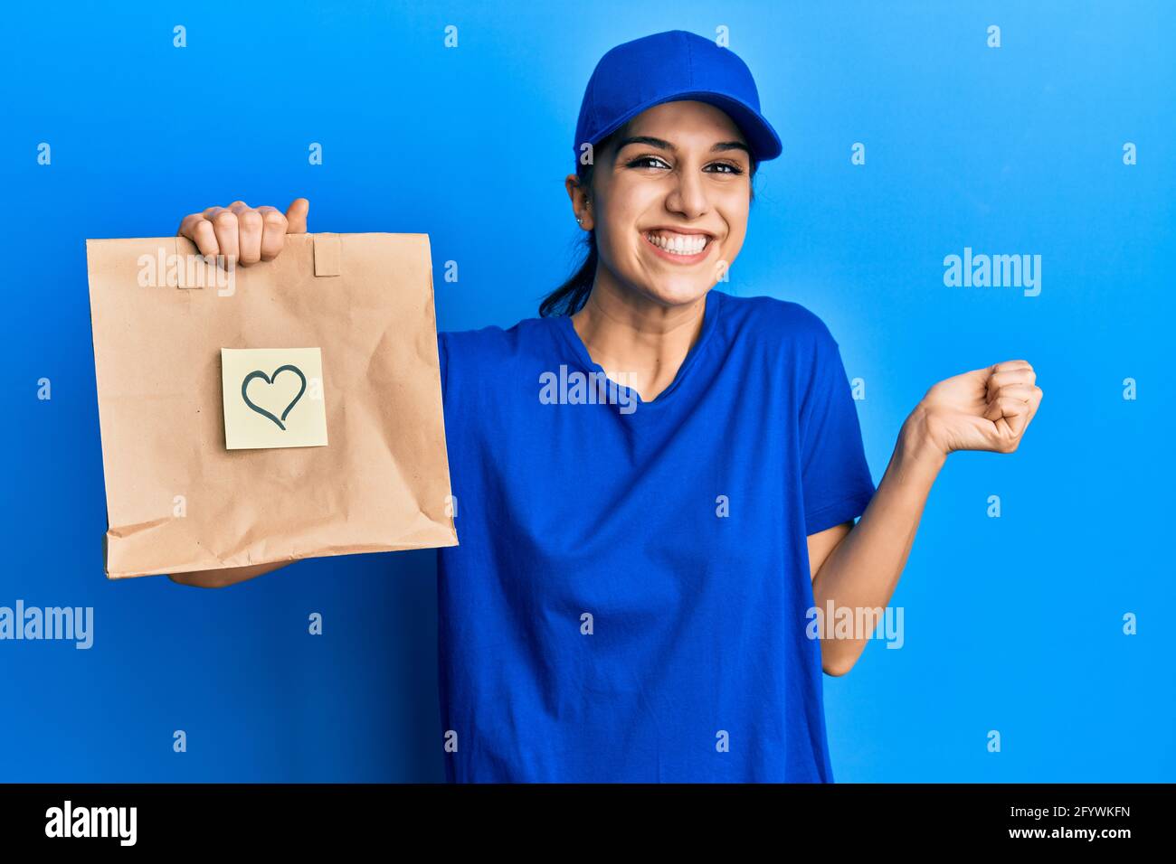 Young hispanic woman holding take away paper bag with heart reminder ...