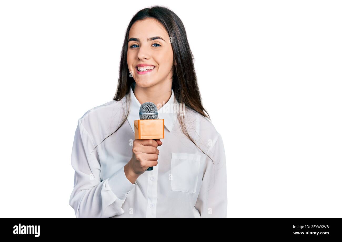 Young brunette teenager holding reporter microphone looking positive ...