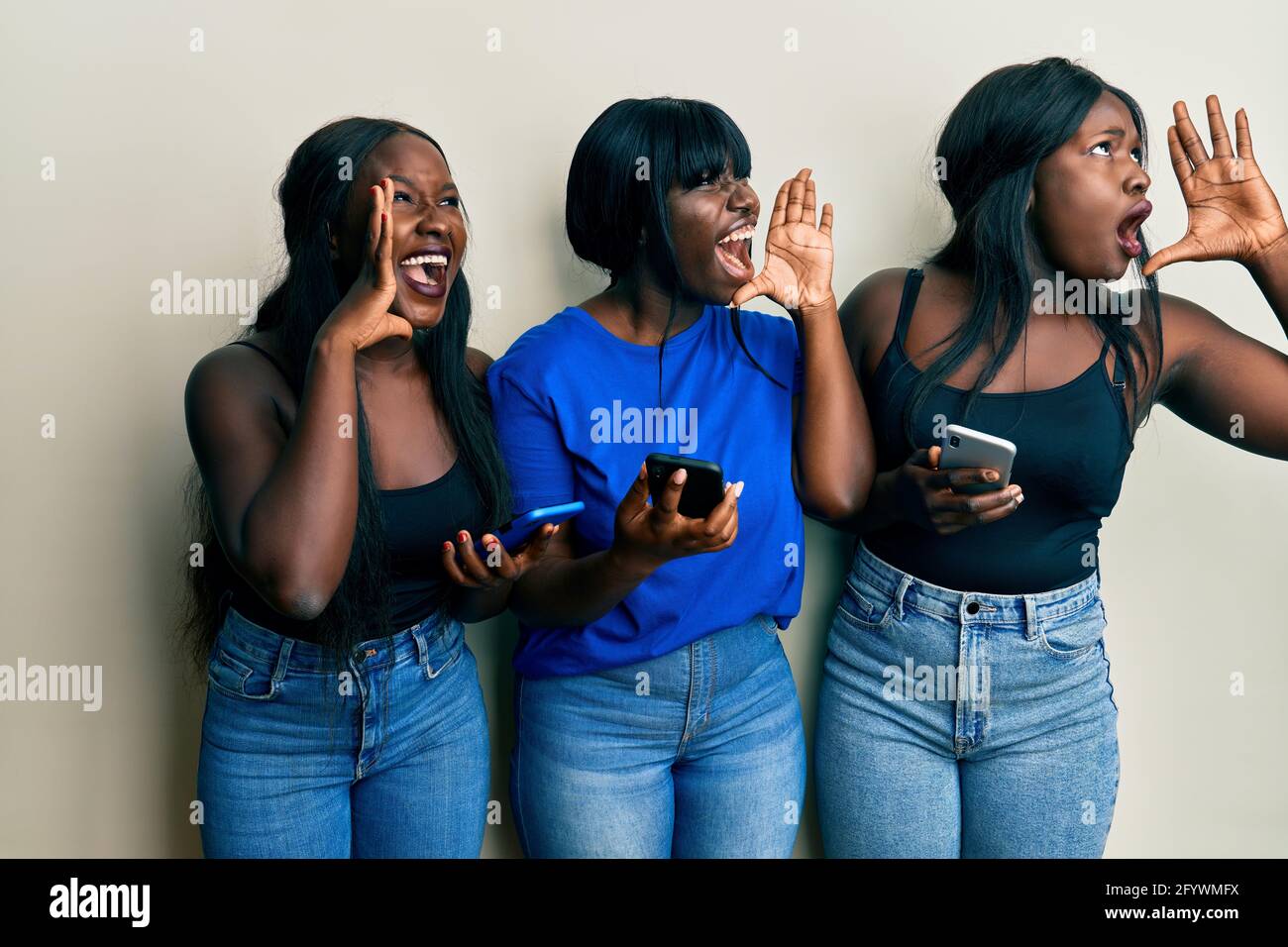 Three young african american friends using smartphone shouting and ...