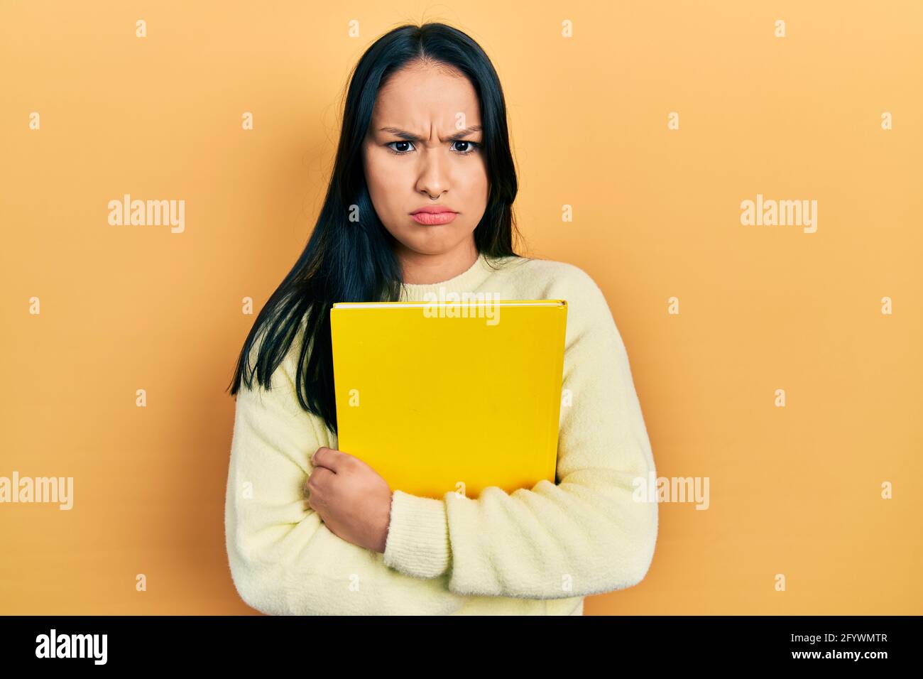 Beautiful hispanic woman with nose piercing holding book skeptic and ...