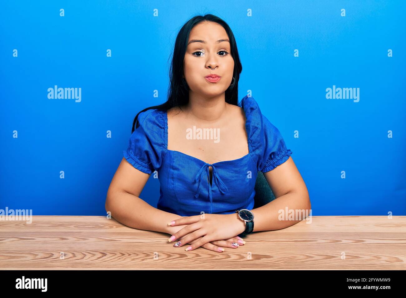 Beautiful hispanic woman with nose piercing sitting on the table ...