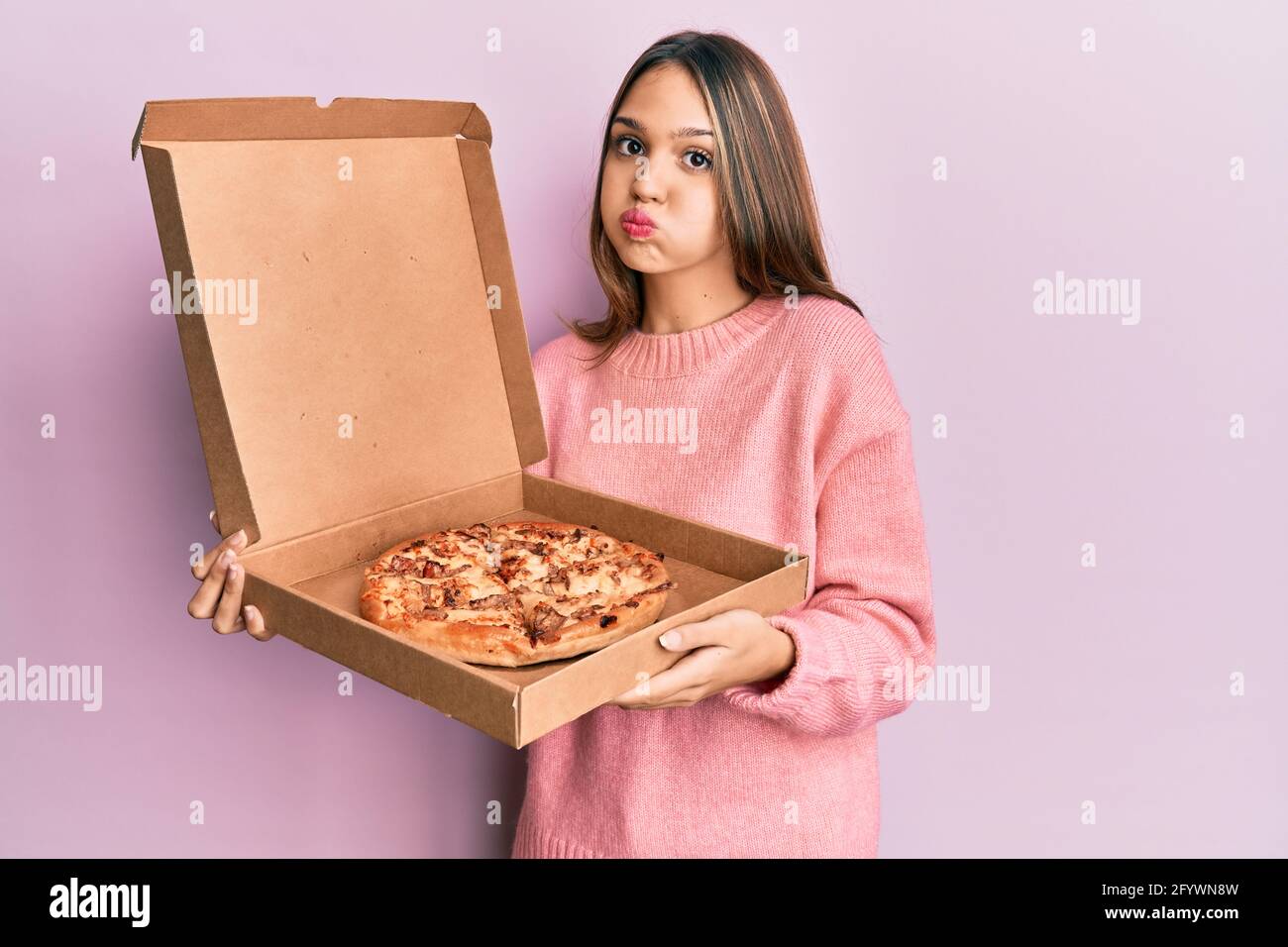 Young brunette woman holding italian pizza puffing cheeks with funny ...