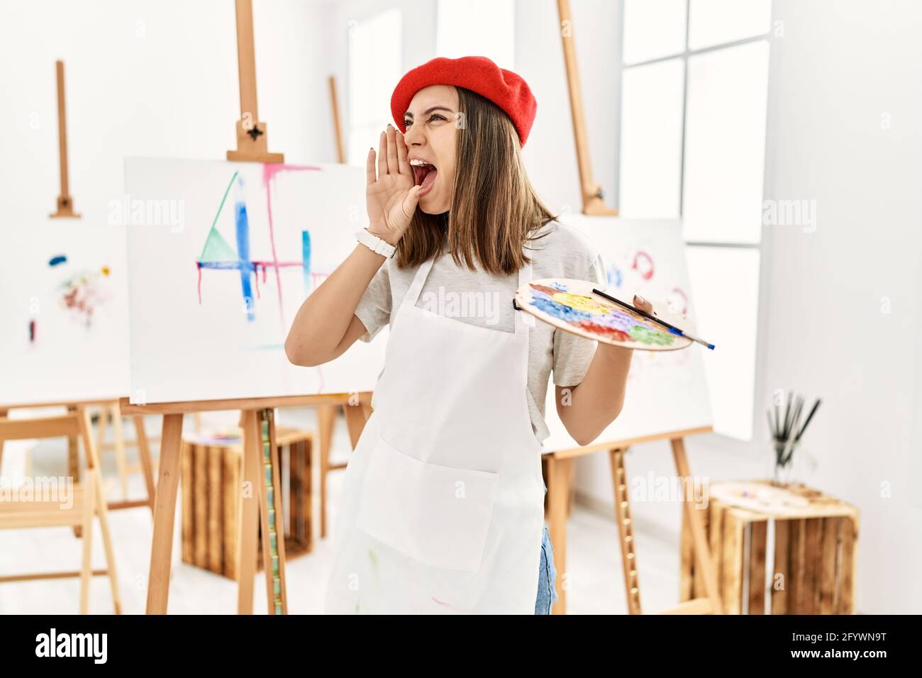 Young artist woman painting on a canvas at art studio shouting and ...