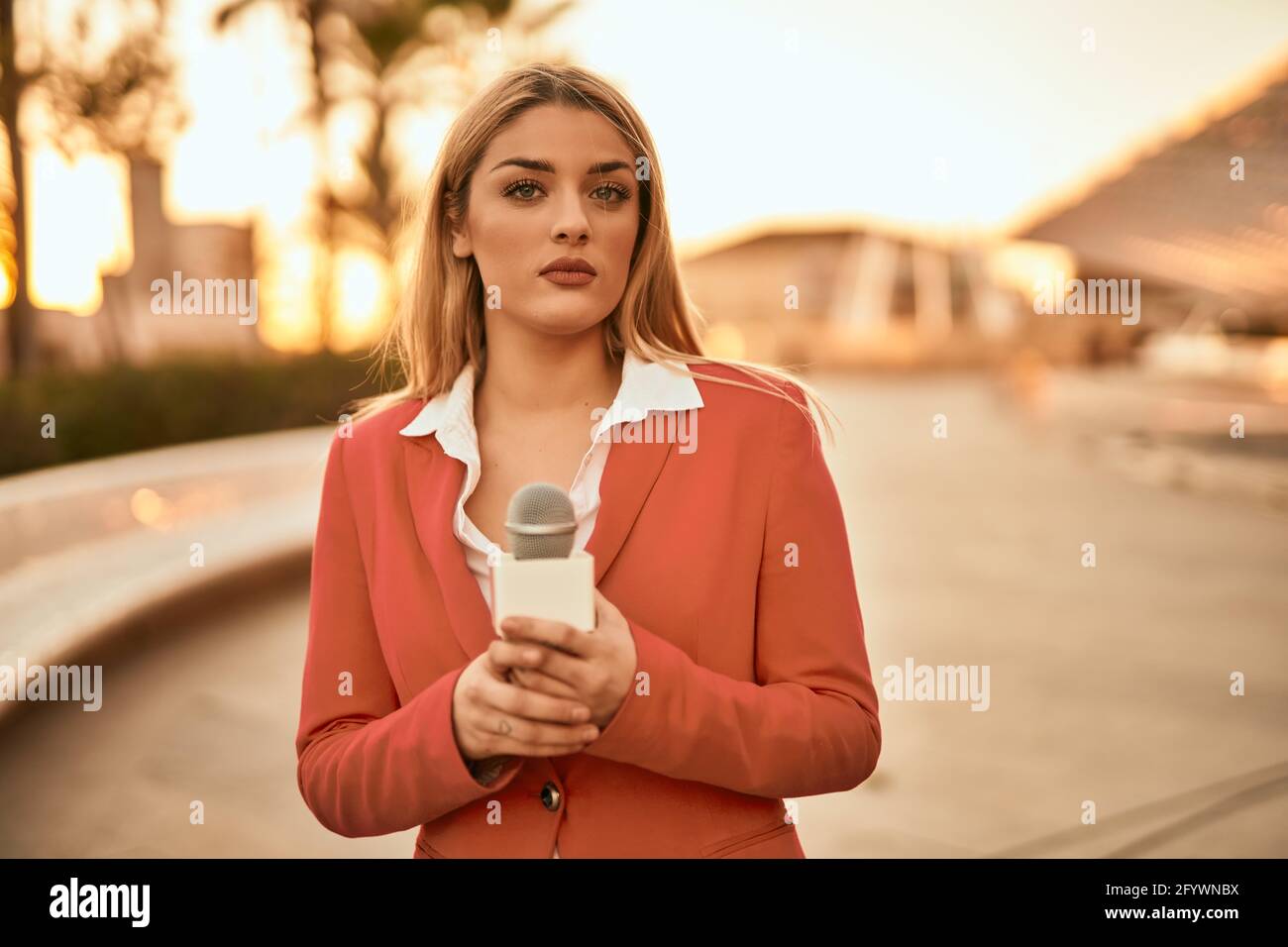 Young blonde reporter woman working using microphone at the city Stock ...