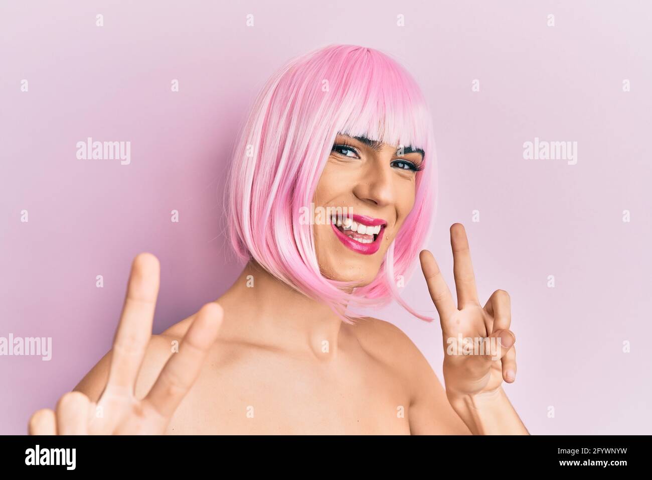 Young man wearing woman make up wearing pink wig smiling looking to the ...