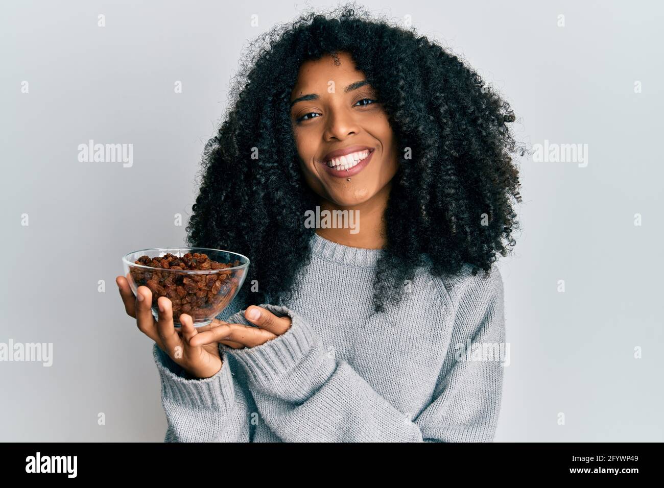 African american woman with afro hair holding raisins in bowl looking ...
