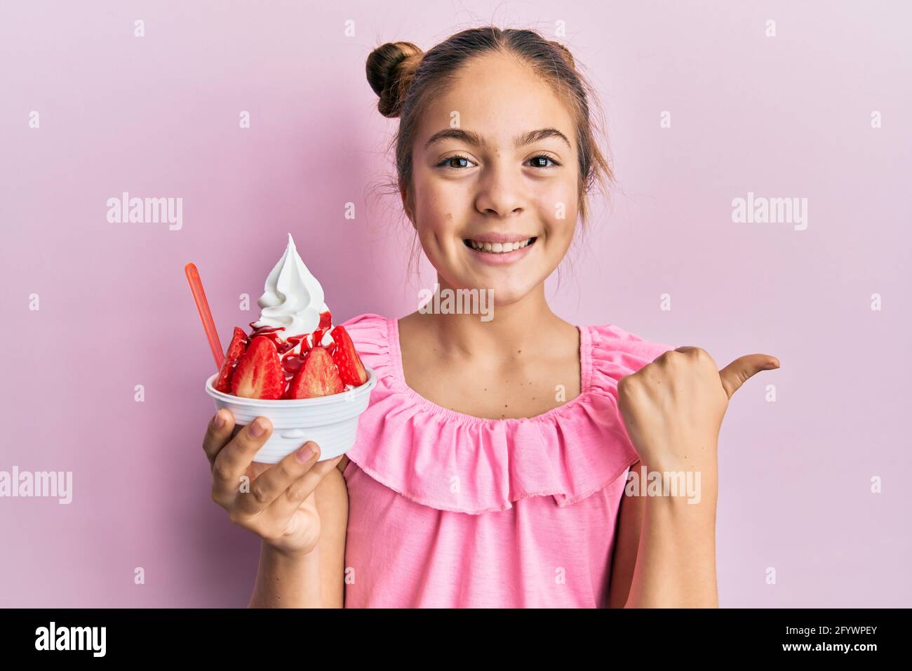 Beautiful brunette little girl eating strawberry ice cream pointing ...