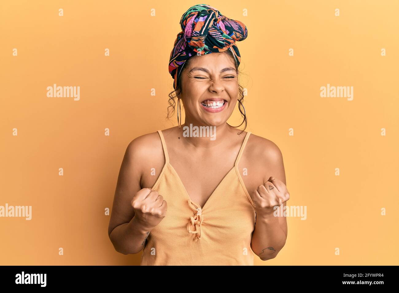 Young hispanic girl wearing hair turban over yellow background excited ...