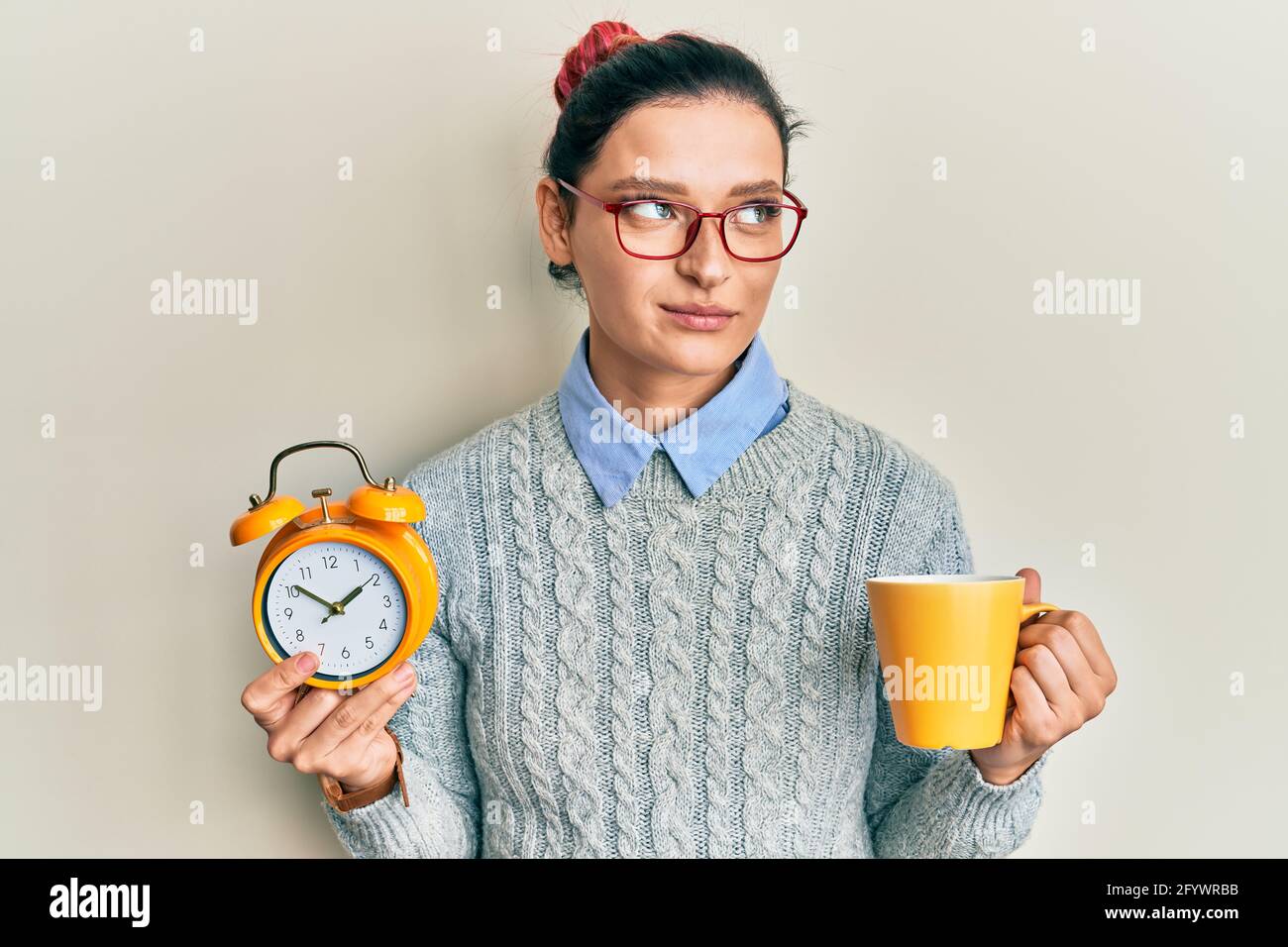Young caucasian woman holding alarm clock drinking coffee smiling ...
