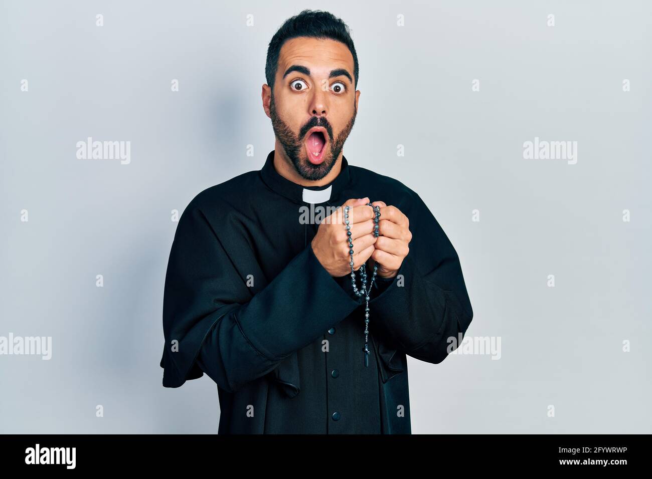 Handsome hispanic priest man with beard praying holding catholic rosary ...