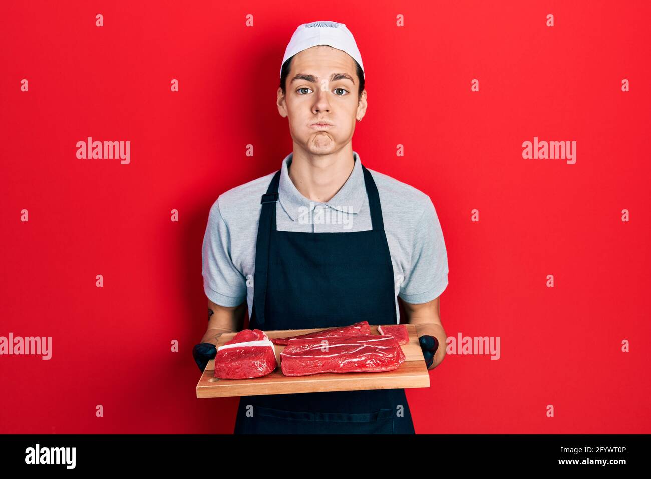 Young hispanic man holding board with raw meat puffing cheeks with ...