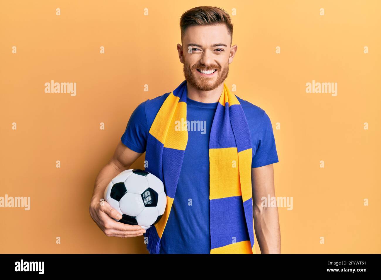 Young redhead man football hooligan holding ball looking positive and ...