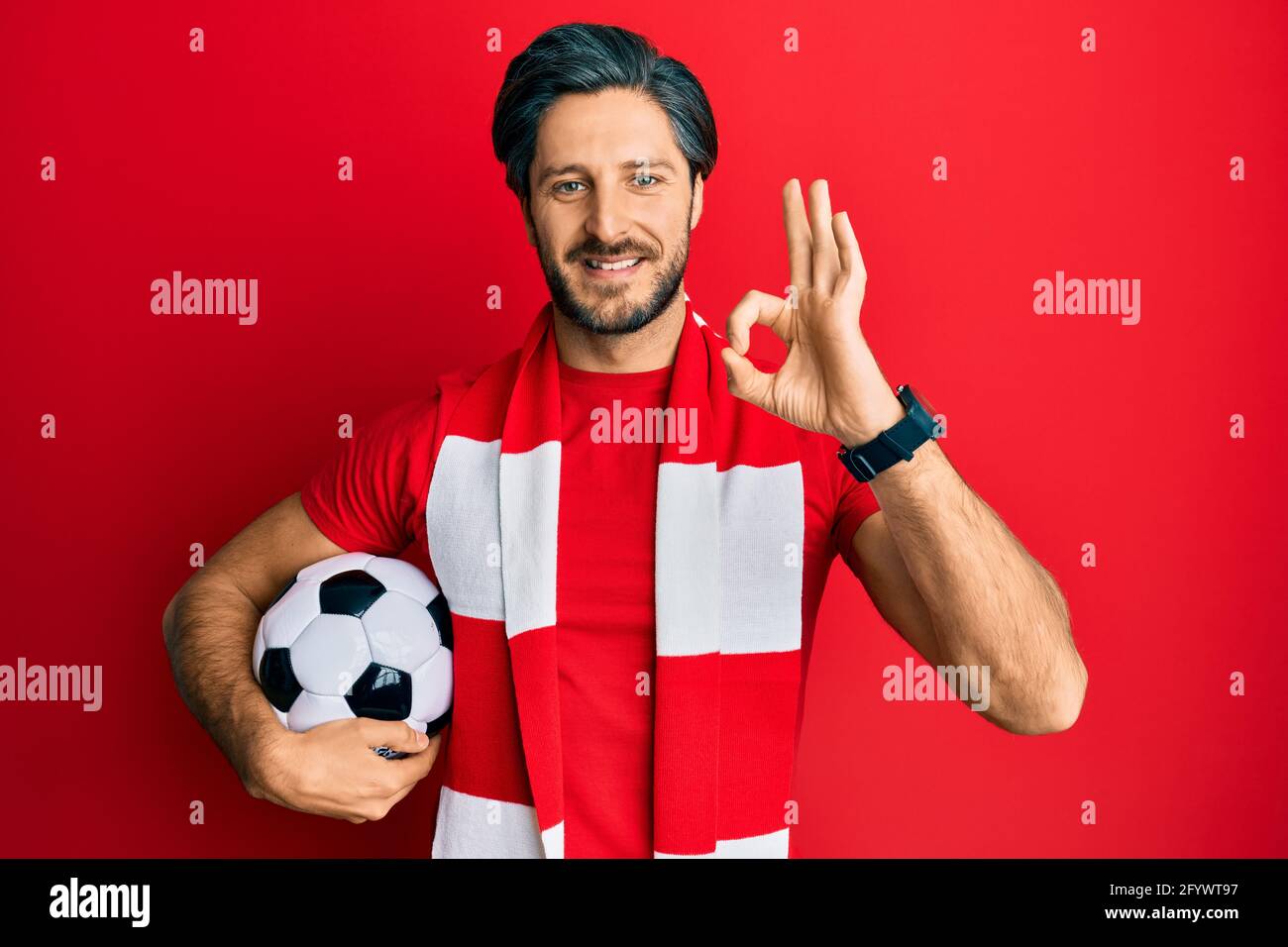 Young hispanic man football hooligan holding ball doing ok sign with ...