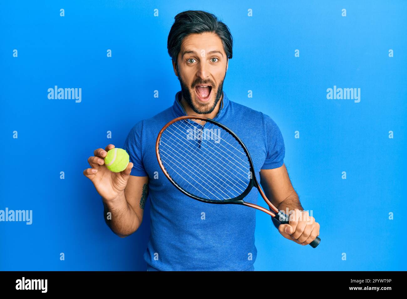 Young hispanic man playing tennis holding racket and ball celebrating ...