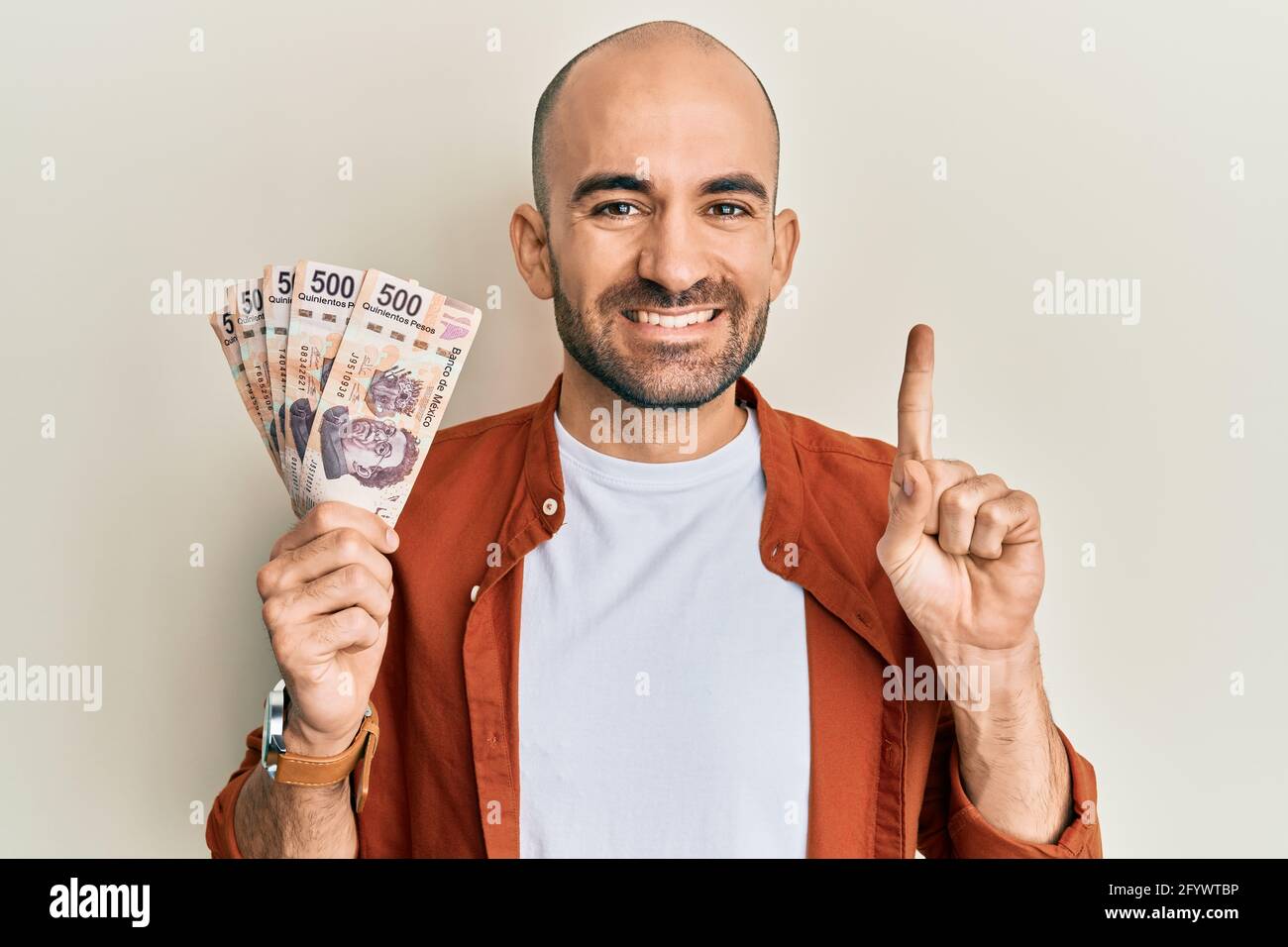 Young hispanic man holding 500 mexican pesos banknotes smiling with an ...