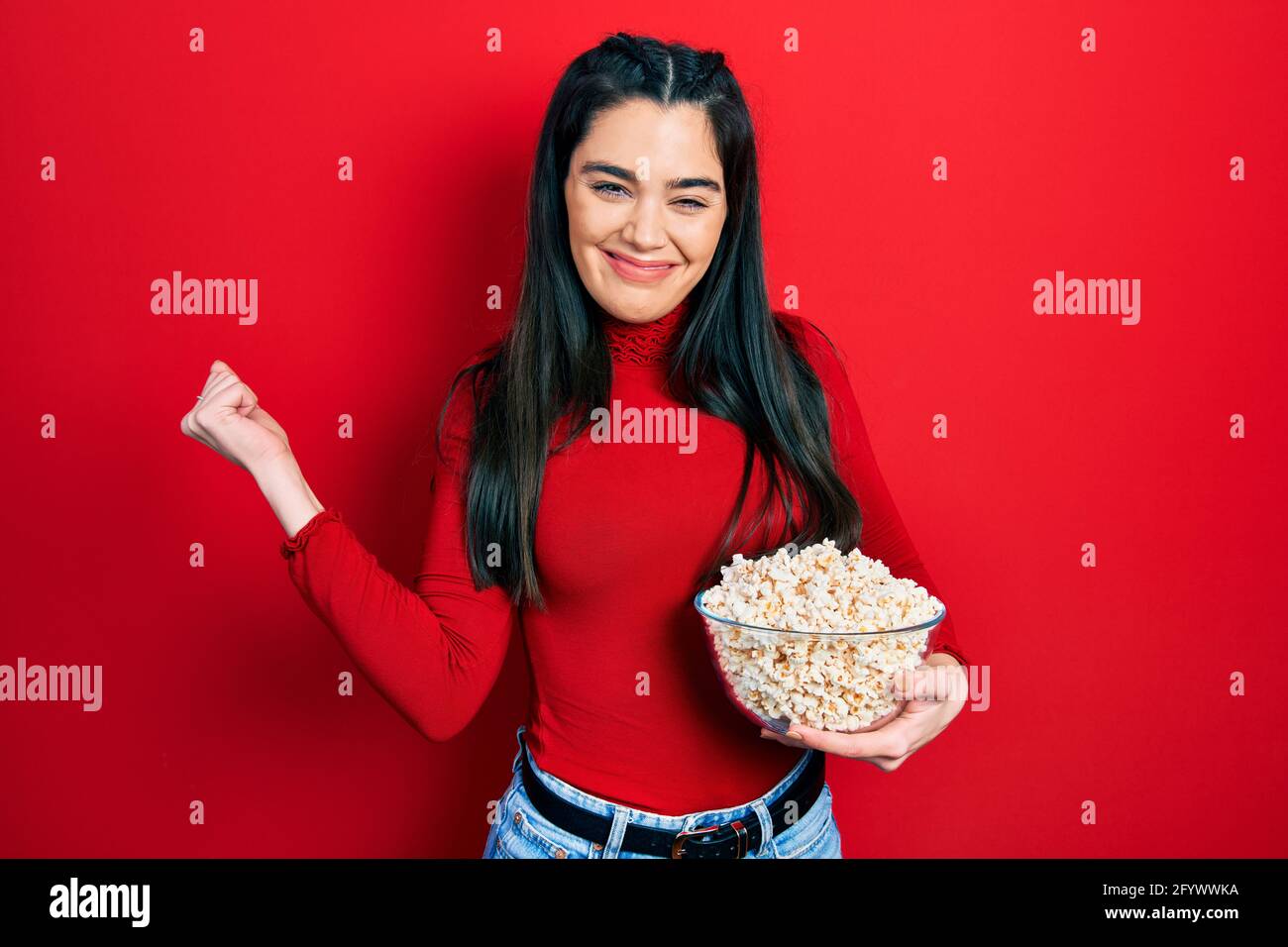 Young hispanic girl eating popcorn screaming proud, celebrating victory ...