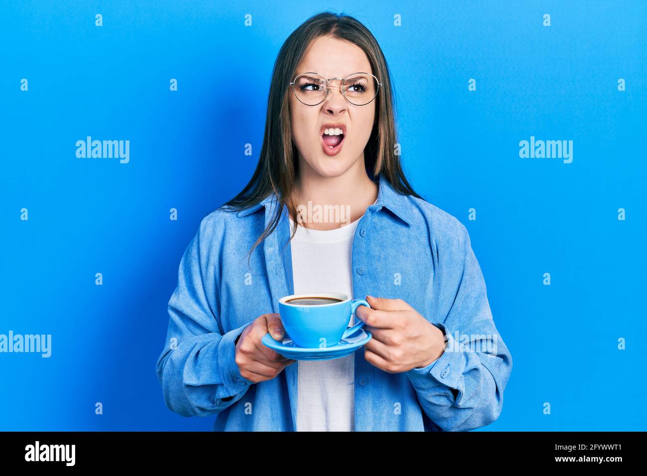 Young hispanic girl drinking a cup of coffee angry and mad screaming ...