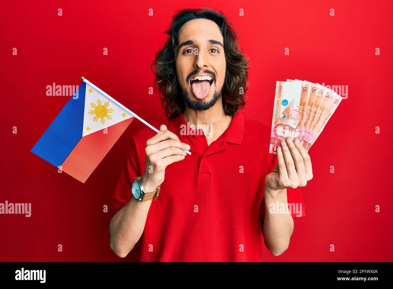 Young hispanic man holding philippines flag and pesos banknotes ...