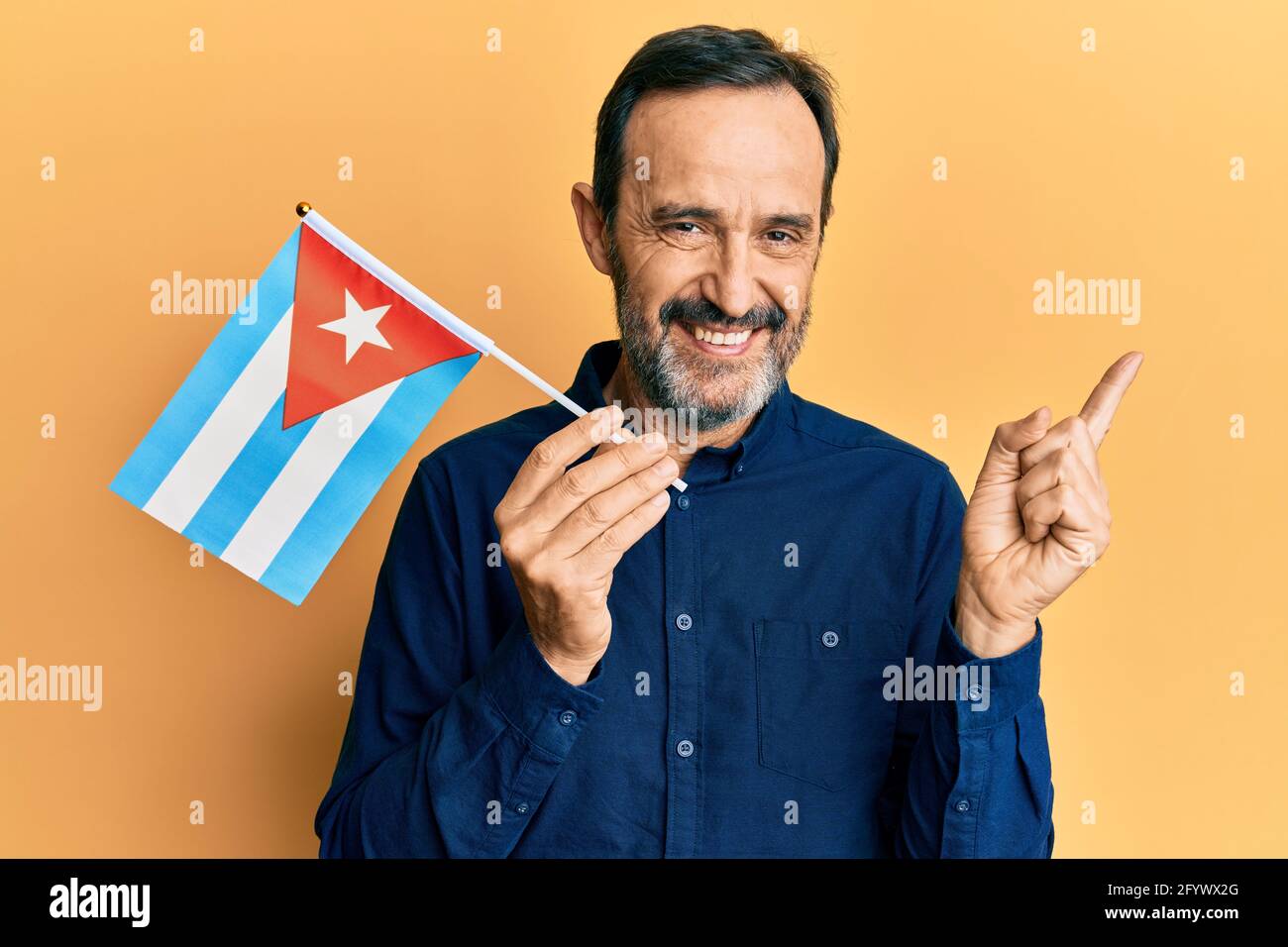 Middle age hispanic man holding cuba flag smiling happy pointing with ...