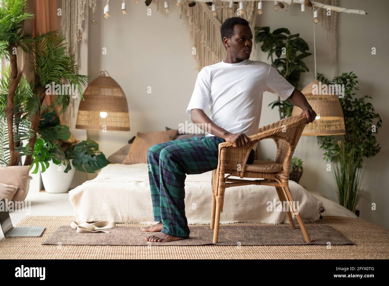 Sporty young african man practicing yoga using chair, doing Revolved ...