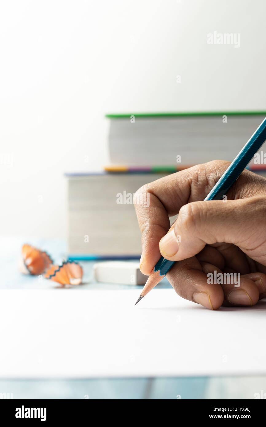 Close up view of hand and pencil writing on paper with books and white ...
