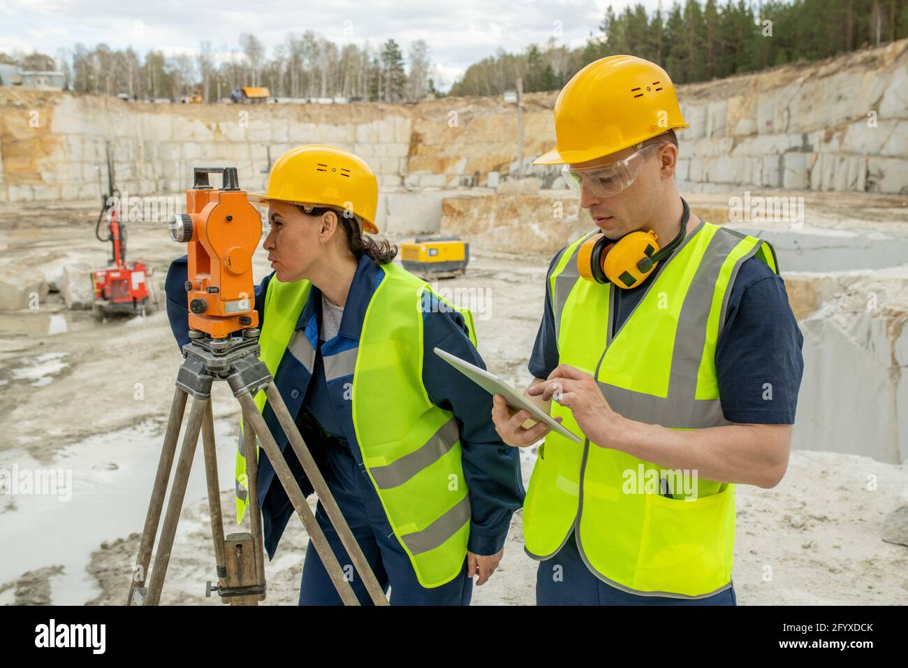 Female engineer using geodetic station while her colleague scrolling in ...