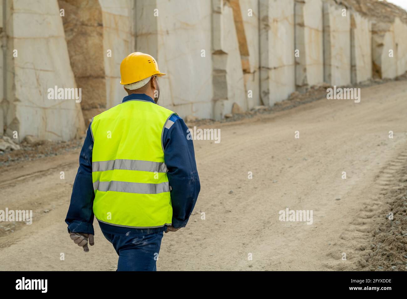Back view of young builder in workwear moving along construction site ...