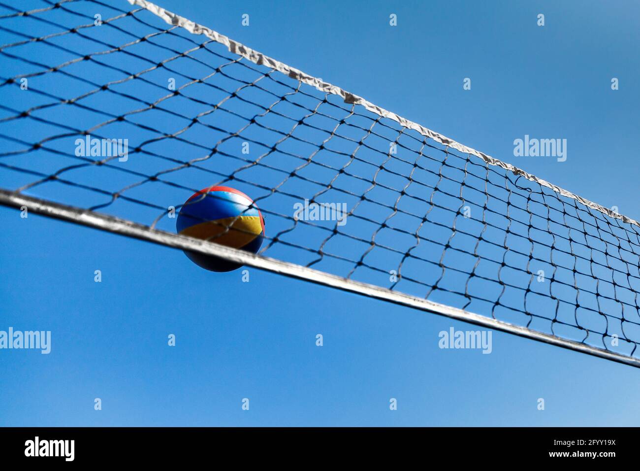 Volleyball ball flying over the volleyball net on a blue summer sky ...