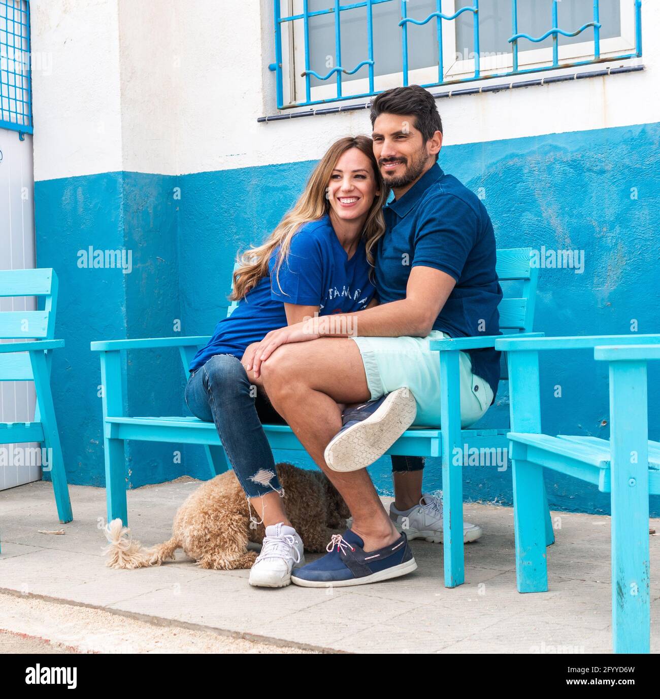 Cheerful ethnic man embracing female beloved on bench against house ...